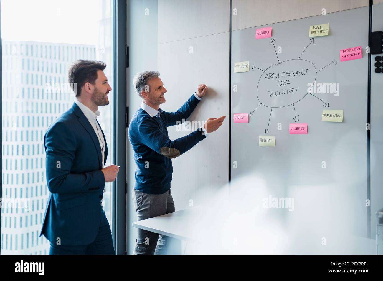 Mature businessman explaining text over whiteboard to male colleague in ...
