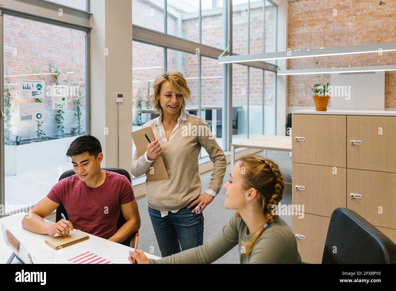 Smiling female professionals discussing by male coworker in coworking office Stock Photo - Alamy