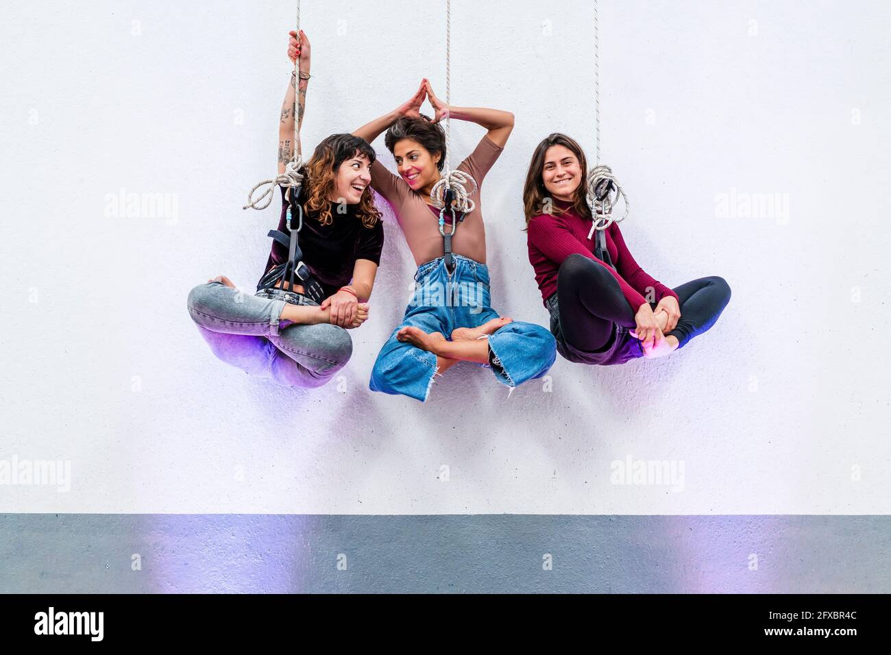 Smiling female acrobats hanging on rope with cross-legged in front of ...