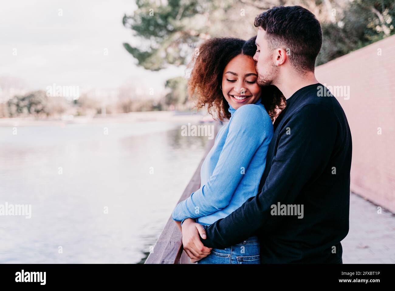 Young boyfriend kissing girlfriend by railing Stock Photo - Alamy