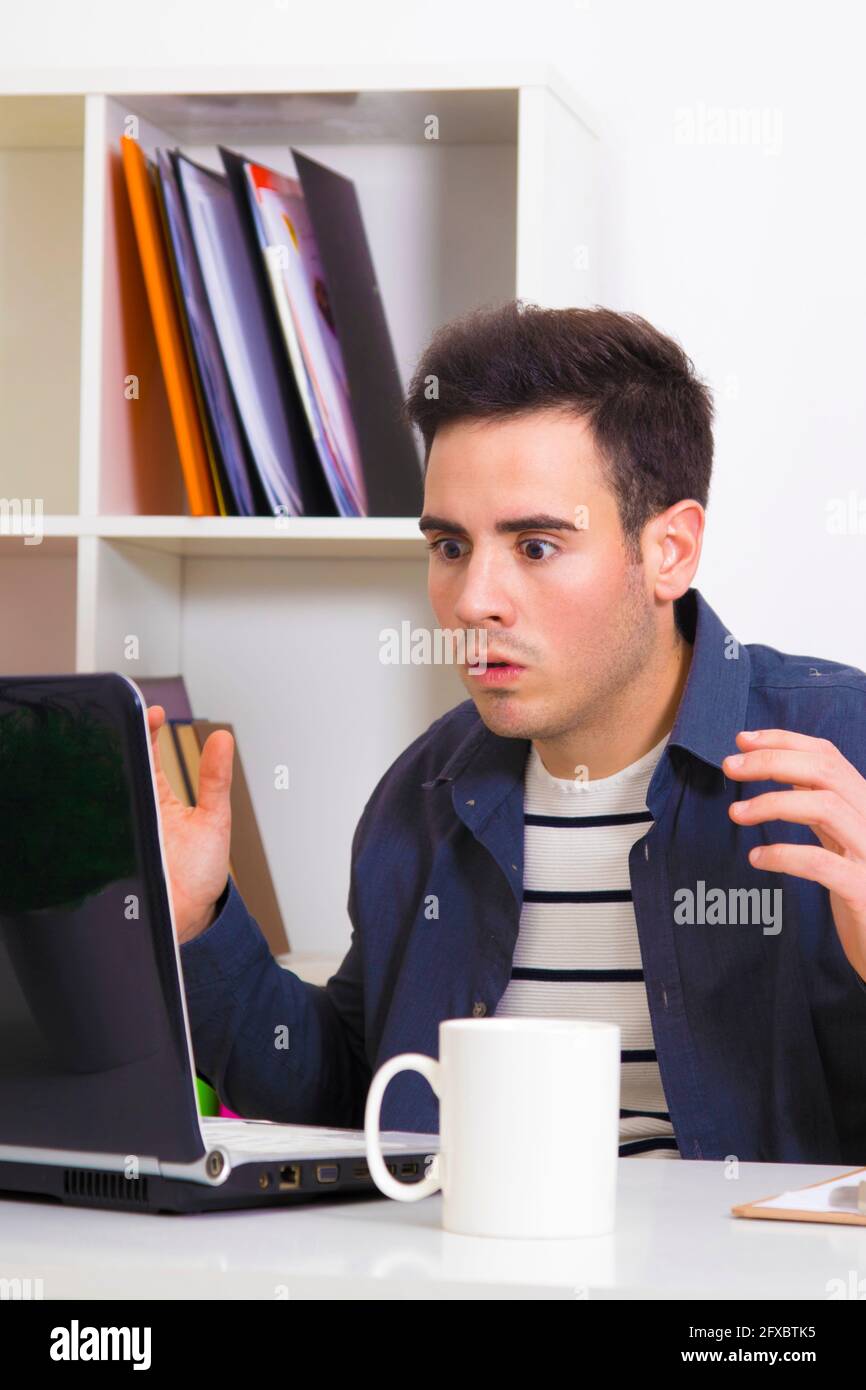 young man surprised looking computer laptop at home or in the office ...