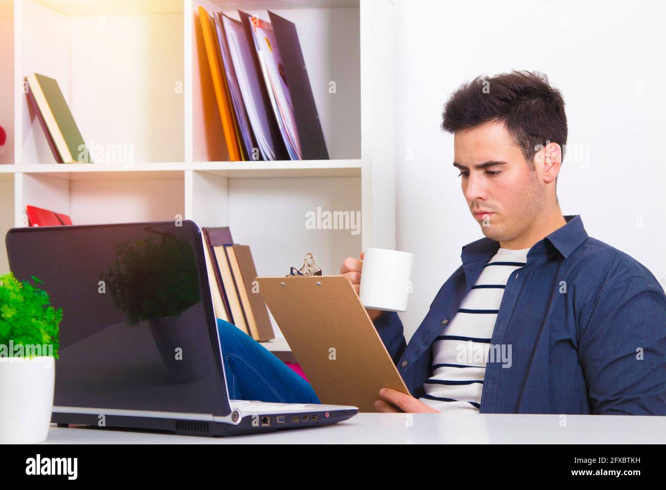 young man reviewing documents having coffee on the desk with laptop ...