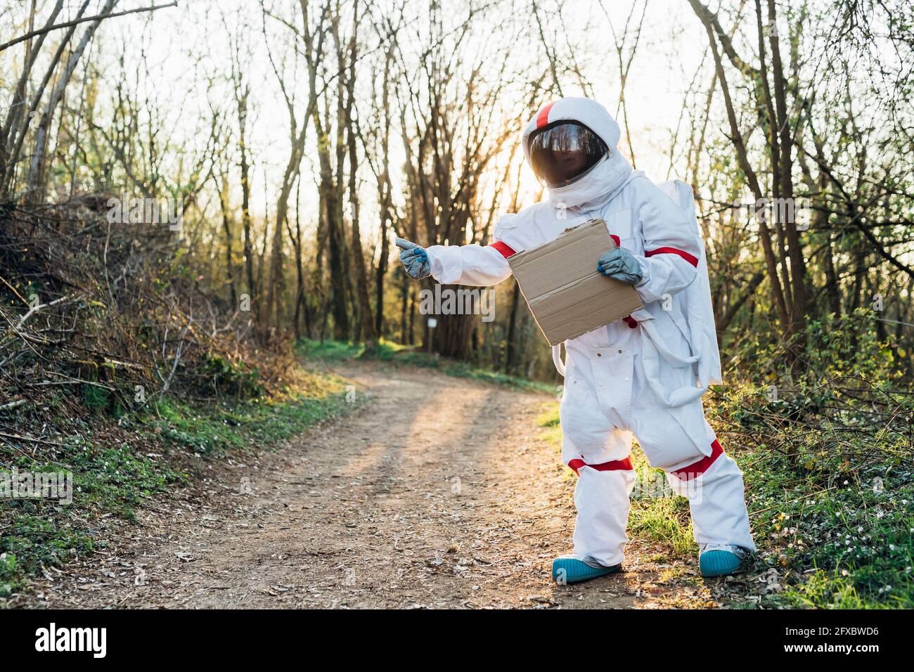 Female explorer in space suit standing with cardboard on dirt road ...