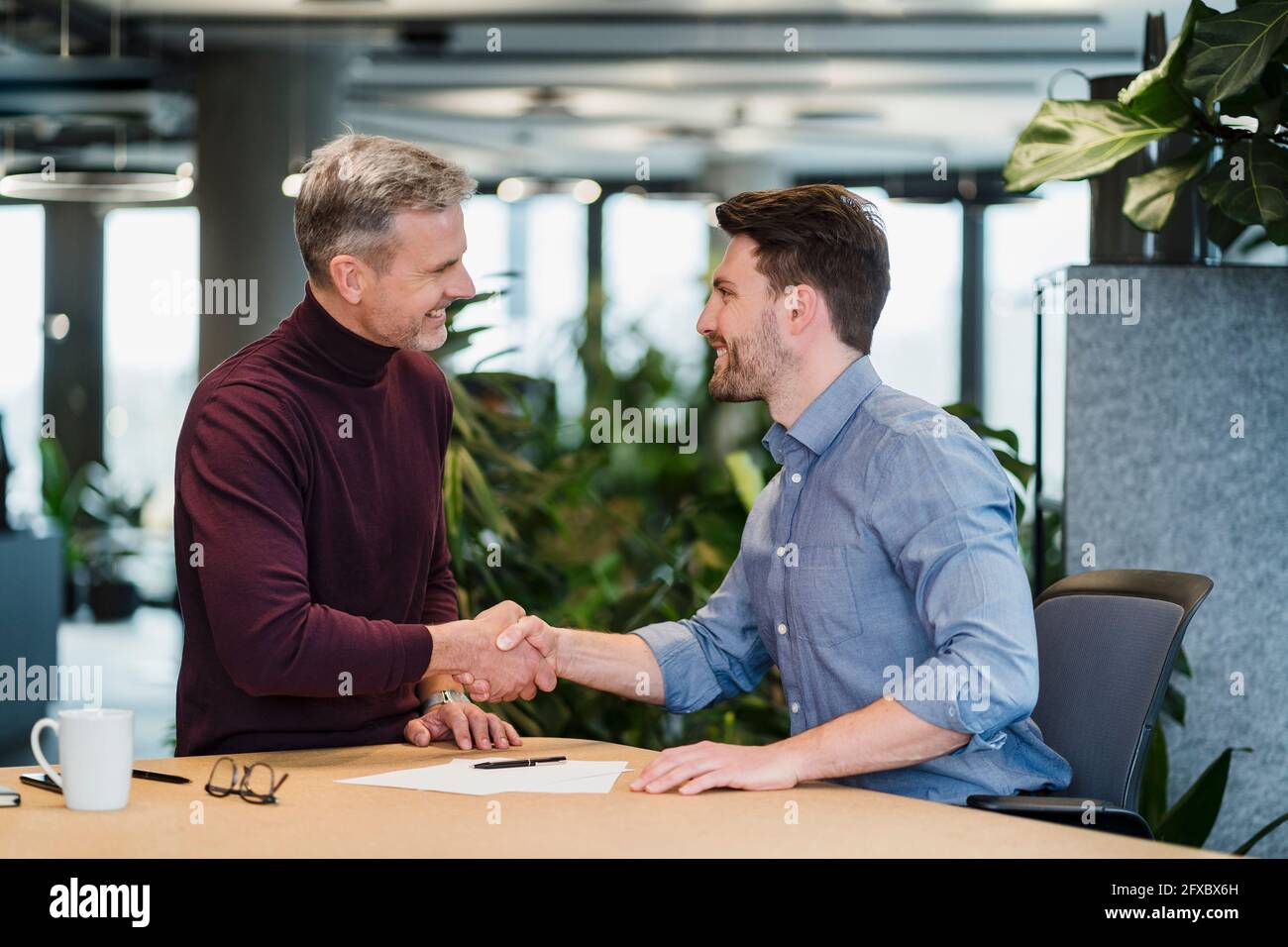 Smiling business people shaking hands at work place Stock Photo - Alamy