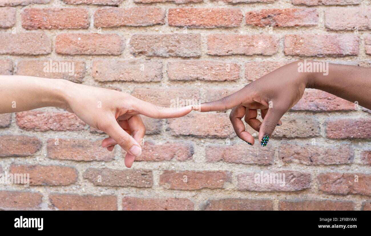 Women touching index fingers by brick wall Stock Photo - Alamy