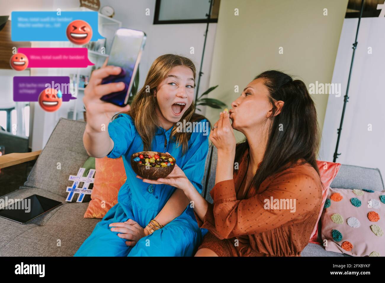 Female influencer filming with friend through mobile phone at home ...