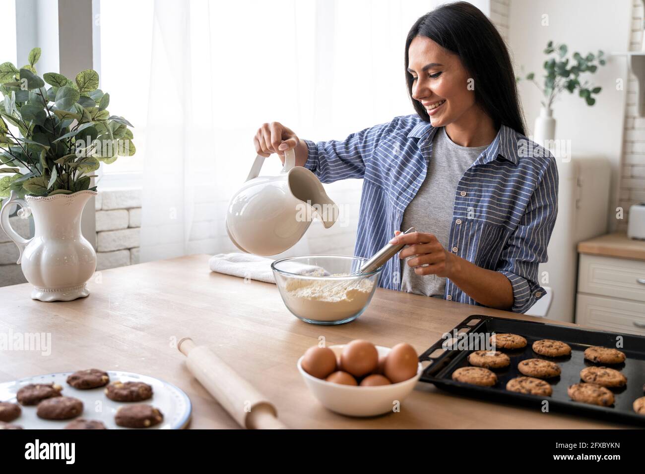Woman pouring water in flour while preparing food in kitchen at home ...