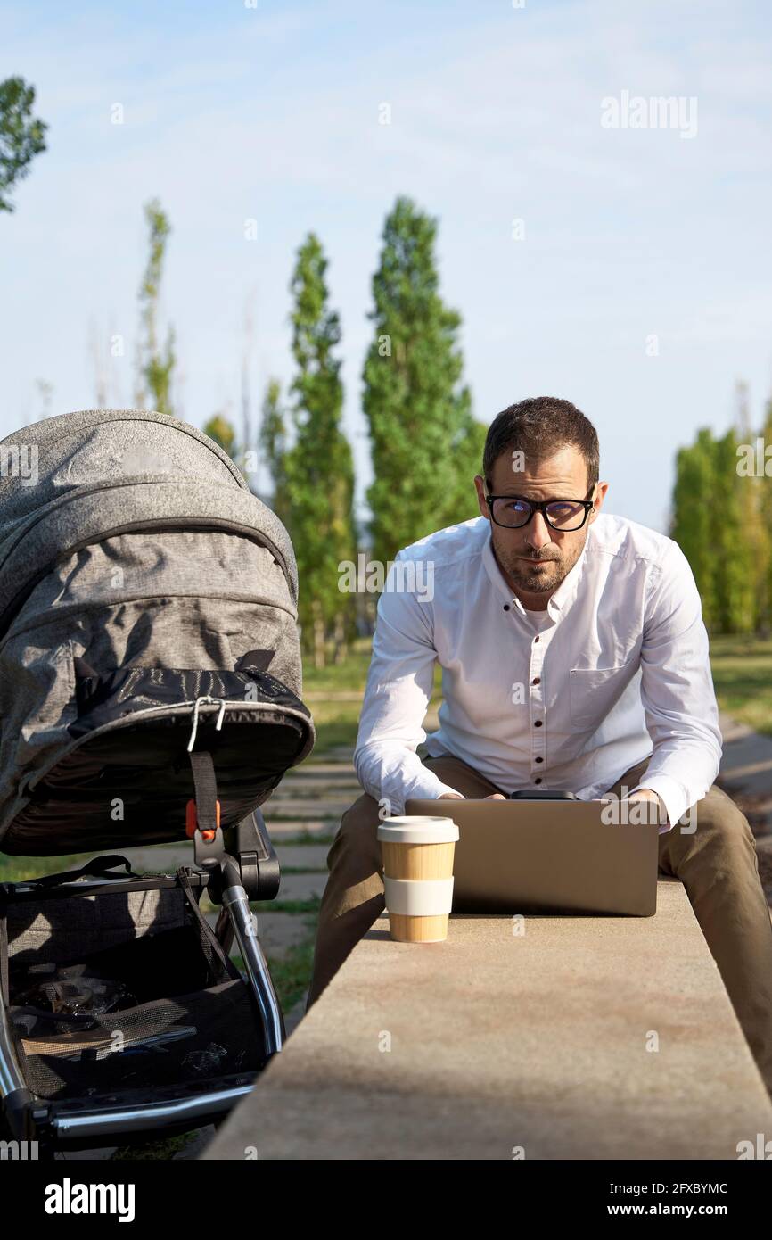 Mid adult male entrepreneur sitting with laptop on retaining wall by ...