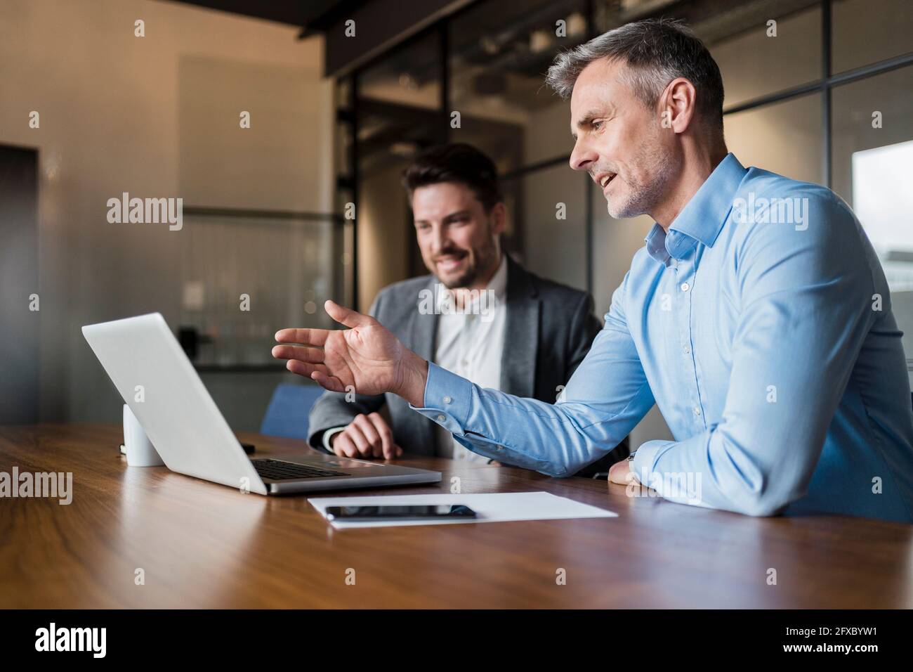 Mature businessman discussing with male colleague over table at work ...