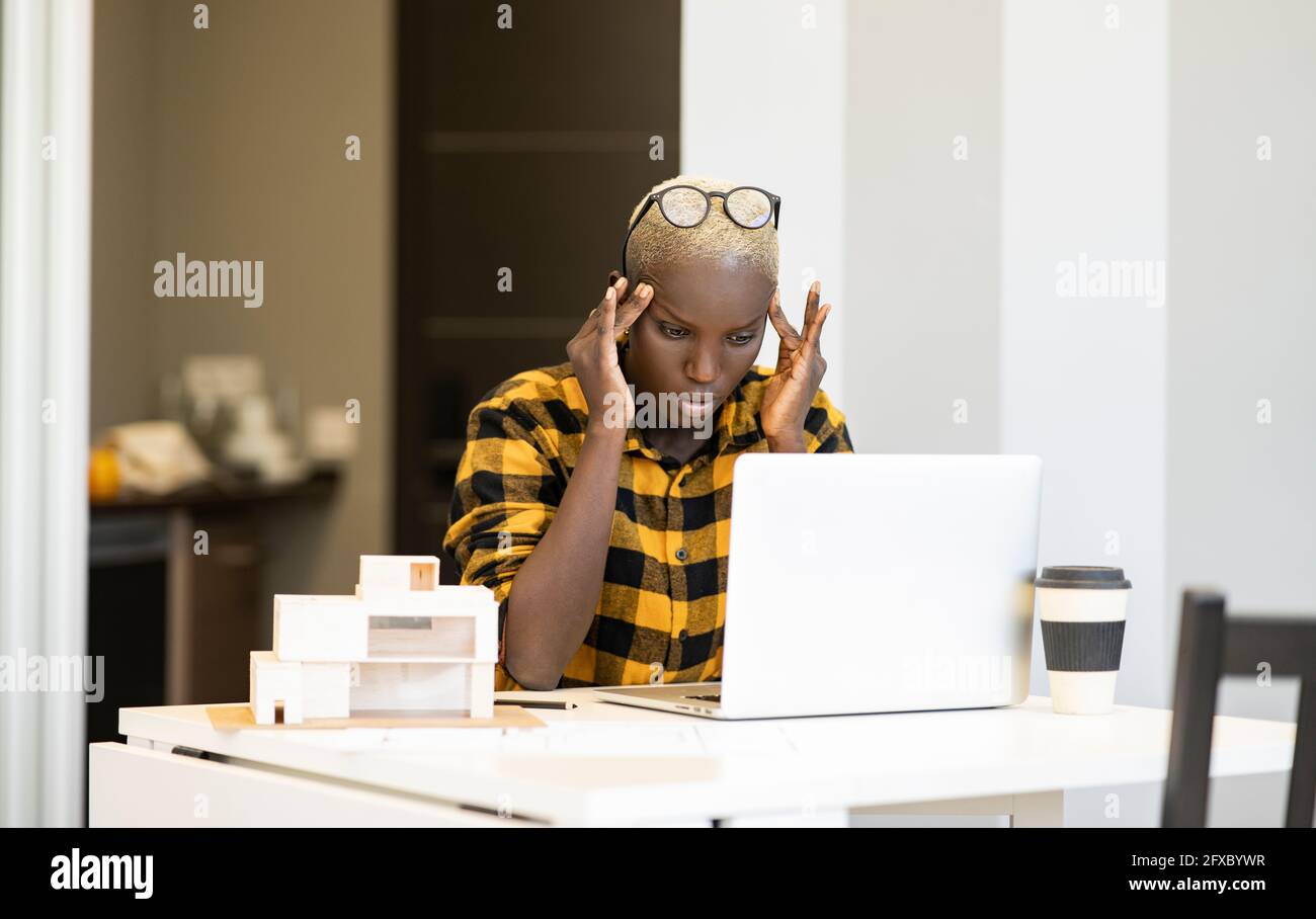 Stressed female architect with head in hands sitting by model at home ...