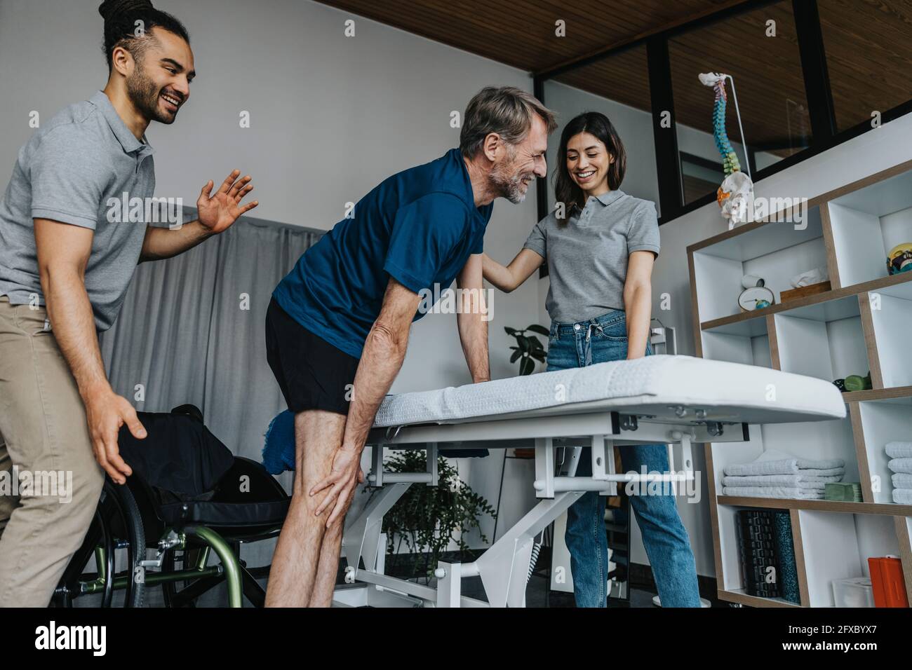 Smiling physiotherapists supporting male patient getting up from ...