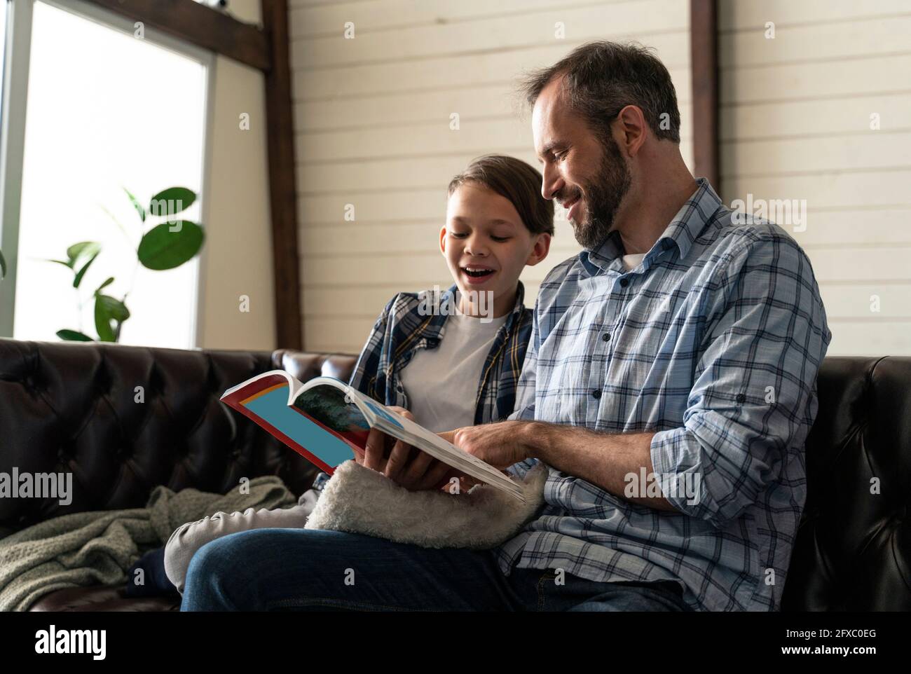 Father and son reading book while sitting at home Stock Photo - Alamy