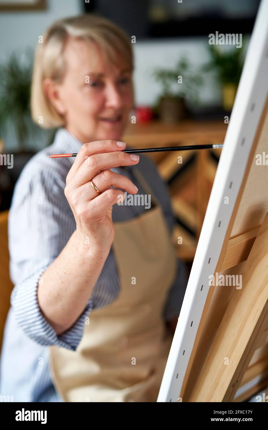 Mature woman making painting on easel at home Stock Photo - Alamy