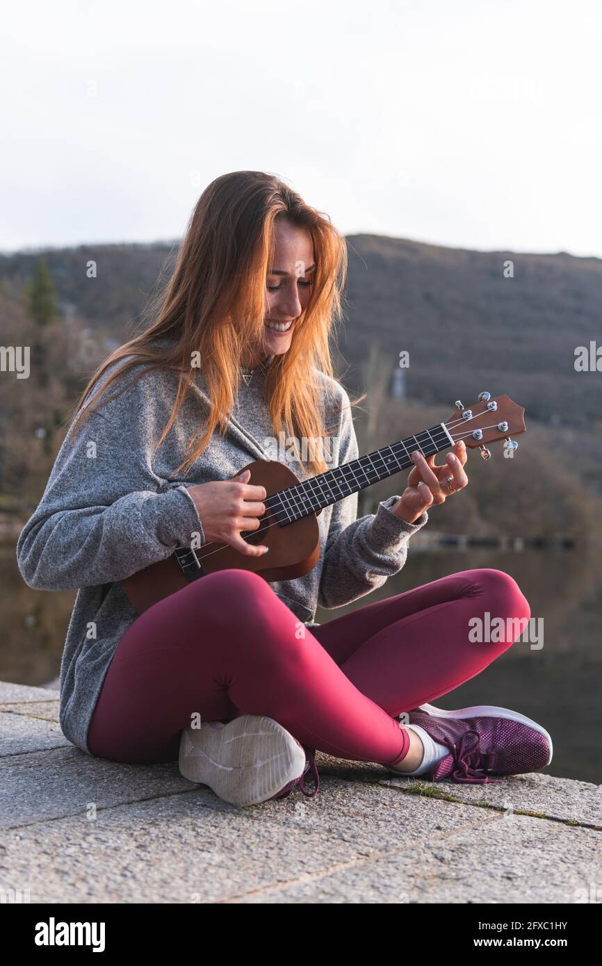 Beautiful woman playing ukulele on while sitting on promenade Stock ...