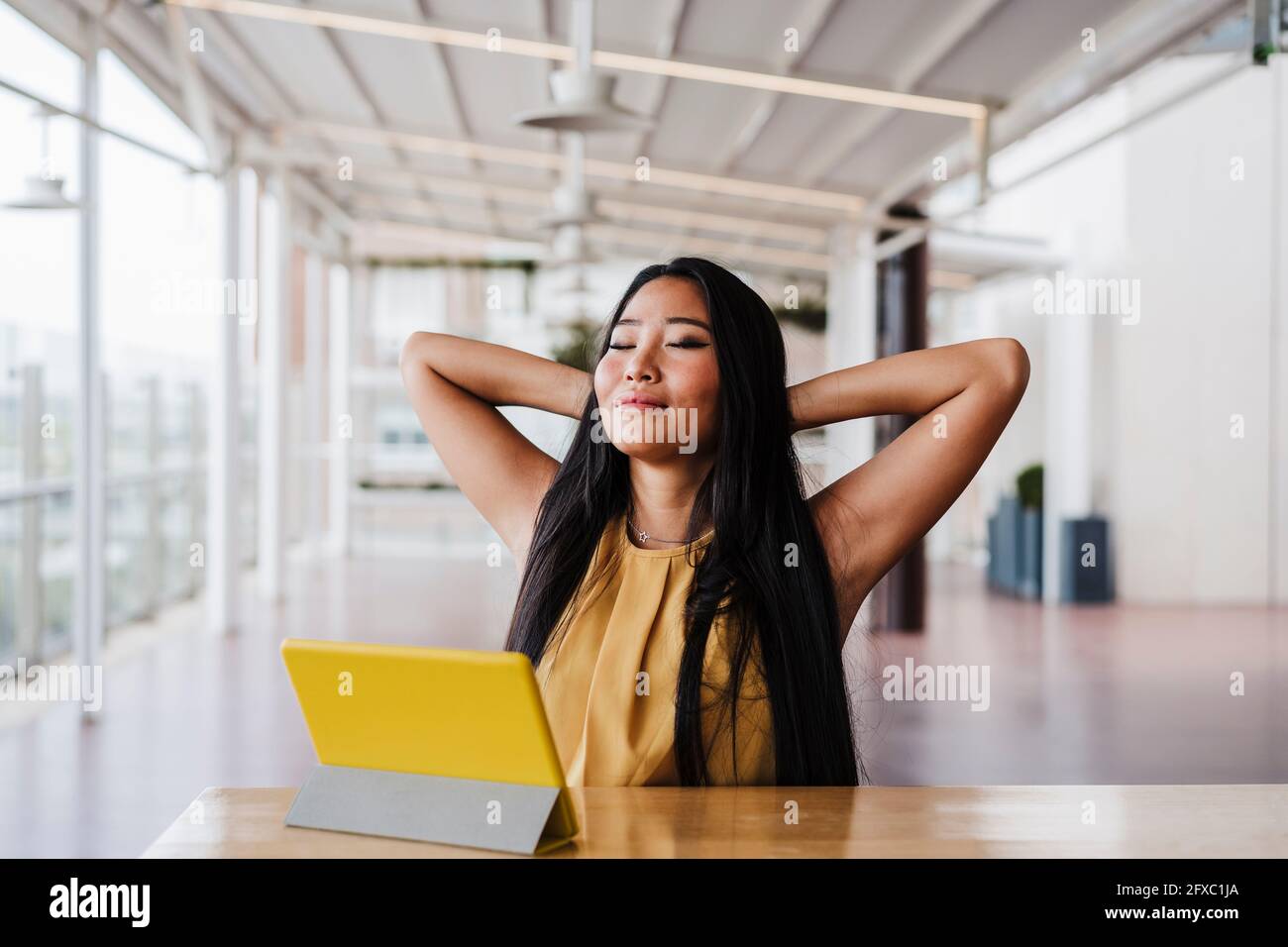 Female professional with hands behind head sitting at table in office ...