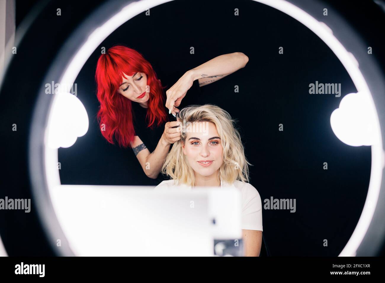 Female stylist doing hairstyle of beautiful model while recording ...