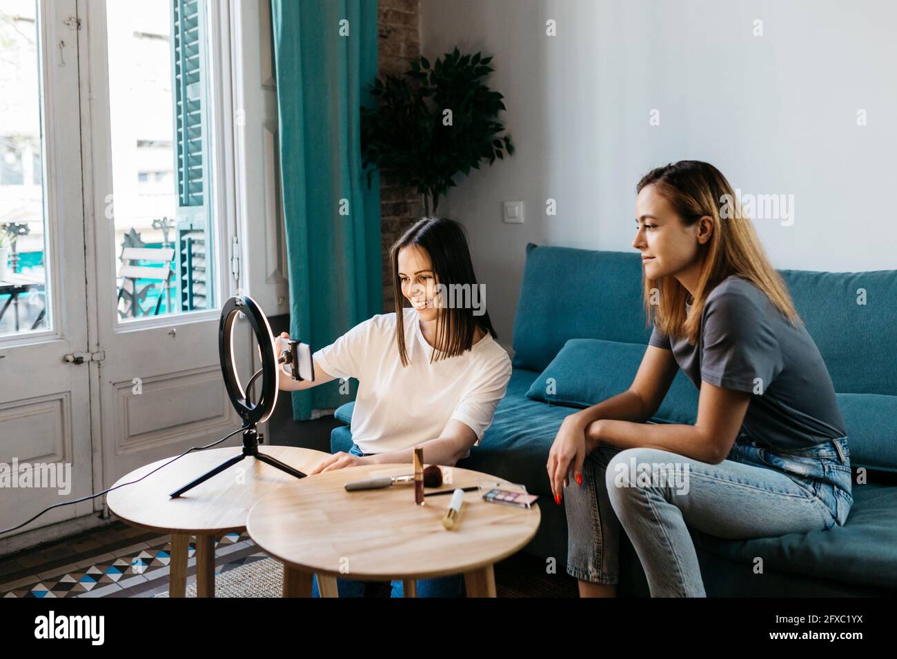 Female influencer vlogging by girlfriend sitting on sofa at home Stock ...