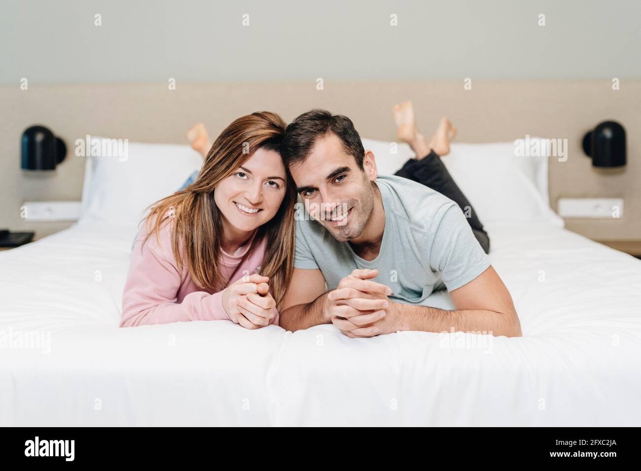 Couple smiling while lying on bed in hotel room Stock Photo - Alamy