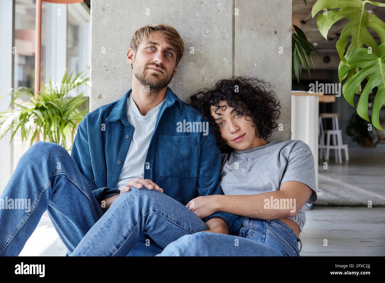 Tired couple leaning on column while sitting on floor at home apartment ...