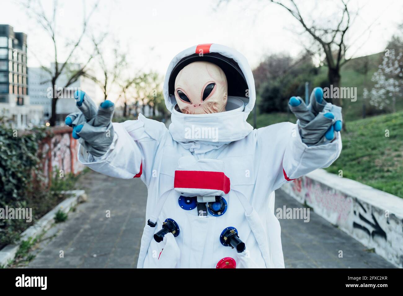 Female astronaut with alien mask showing peace sign while standing on ...