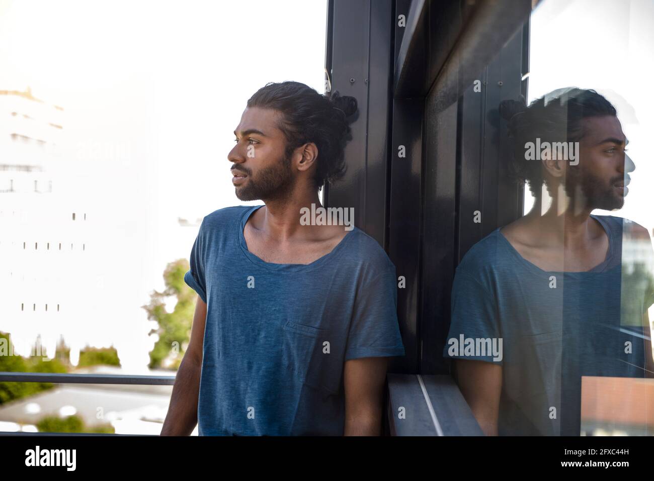 Young man leaning on glass wall in balcony during break Stock Photo - Alamy