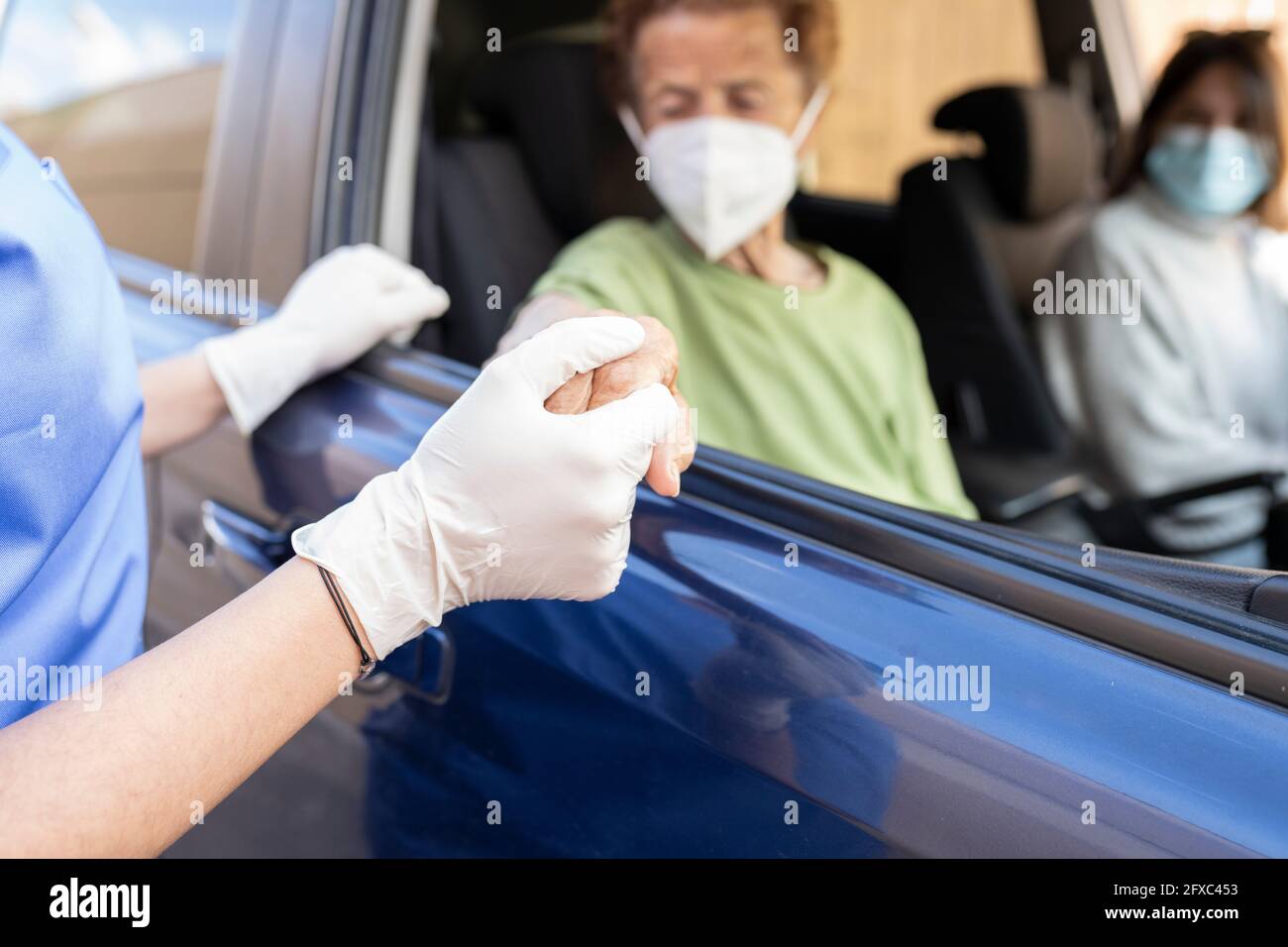 Female healthcare worker holding hand of senior patient sitting in car ...