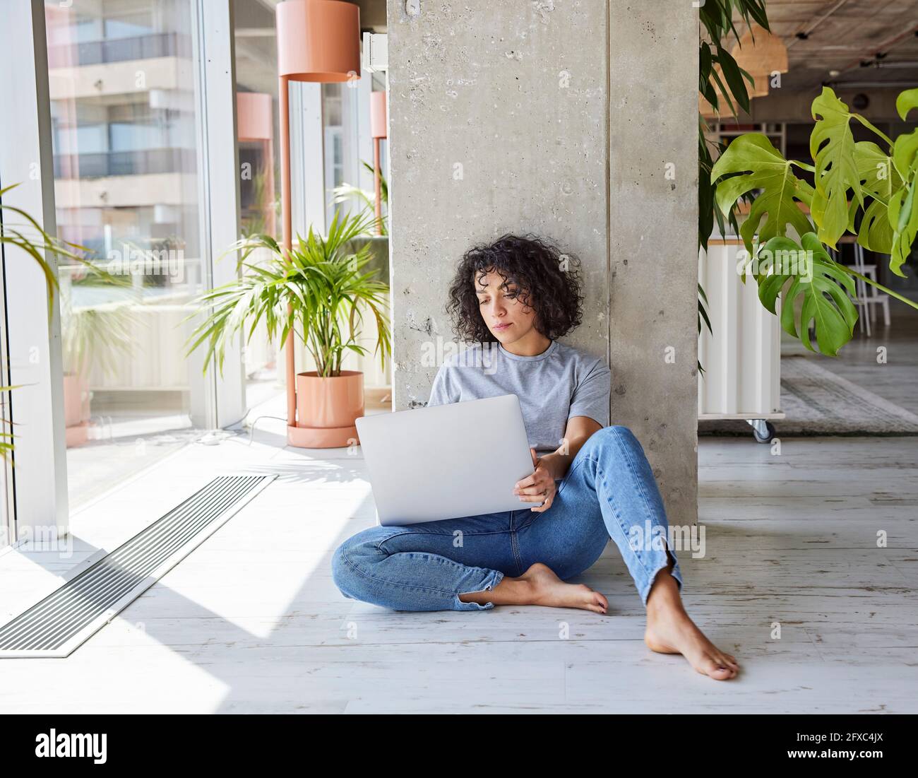 Curly haired woman sitting on floor in front of column at home ...