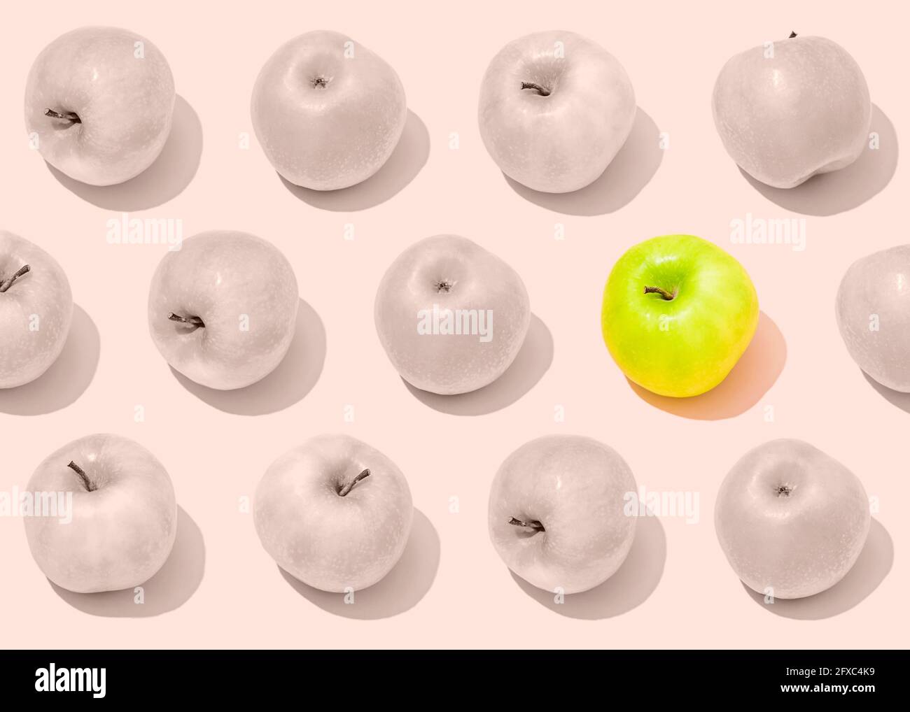Pattern of rows of bland light pink apples with single vibrant green ...