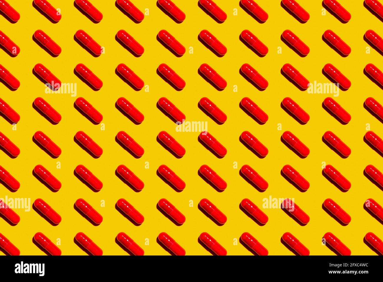 Pattern of rows of red medicine capsules laid against yellow background ...