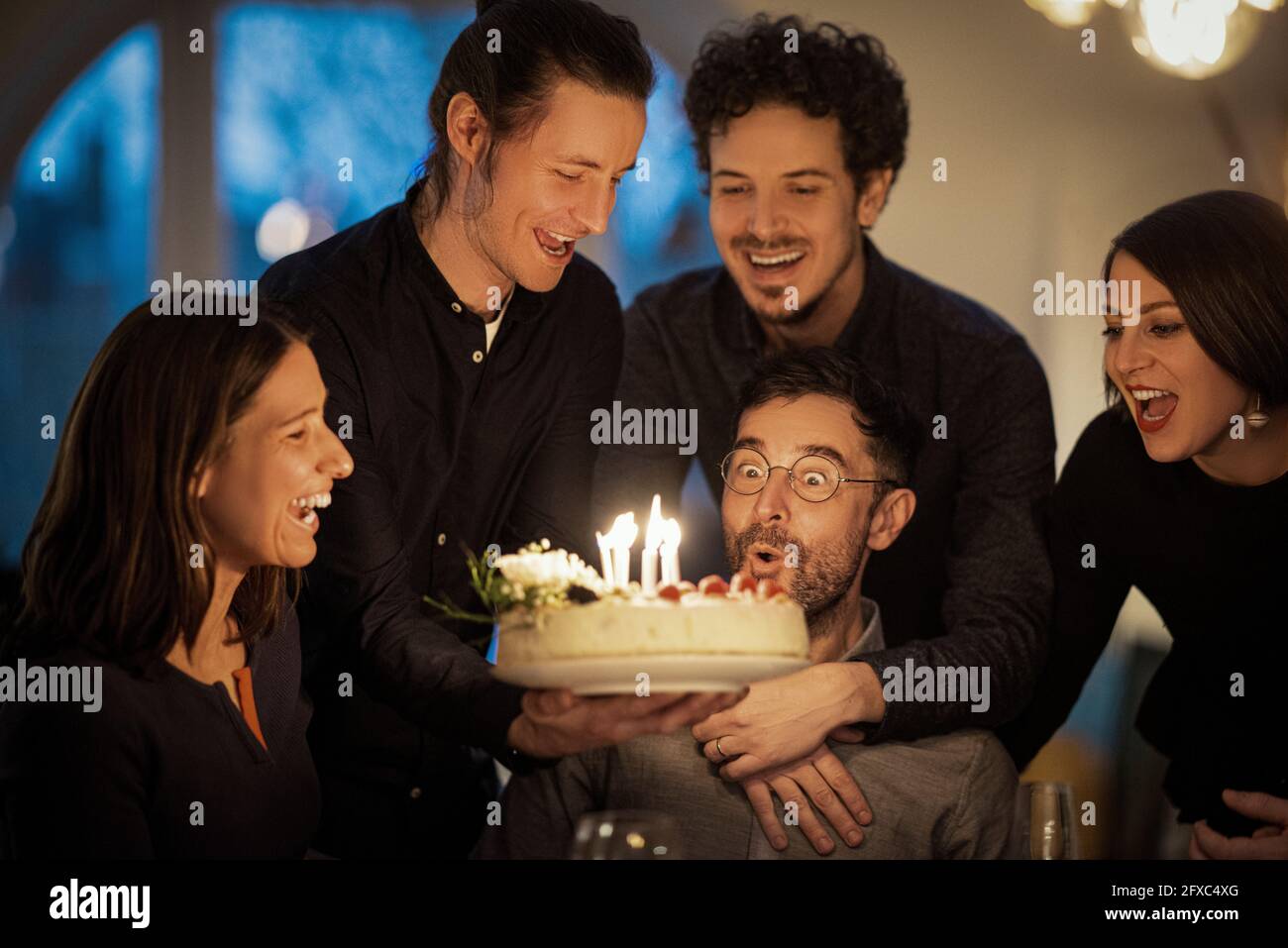 Surprised man looking at birthday cake amidst male and female friends ...