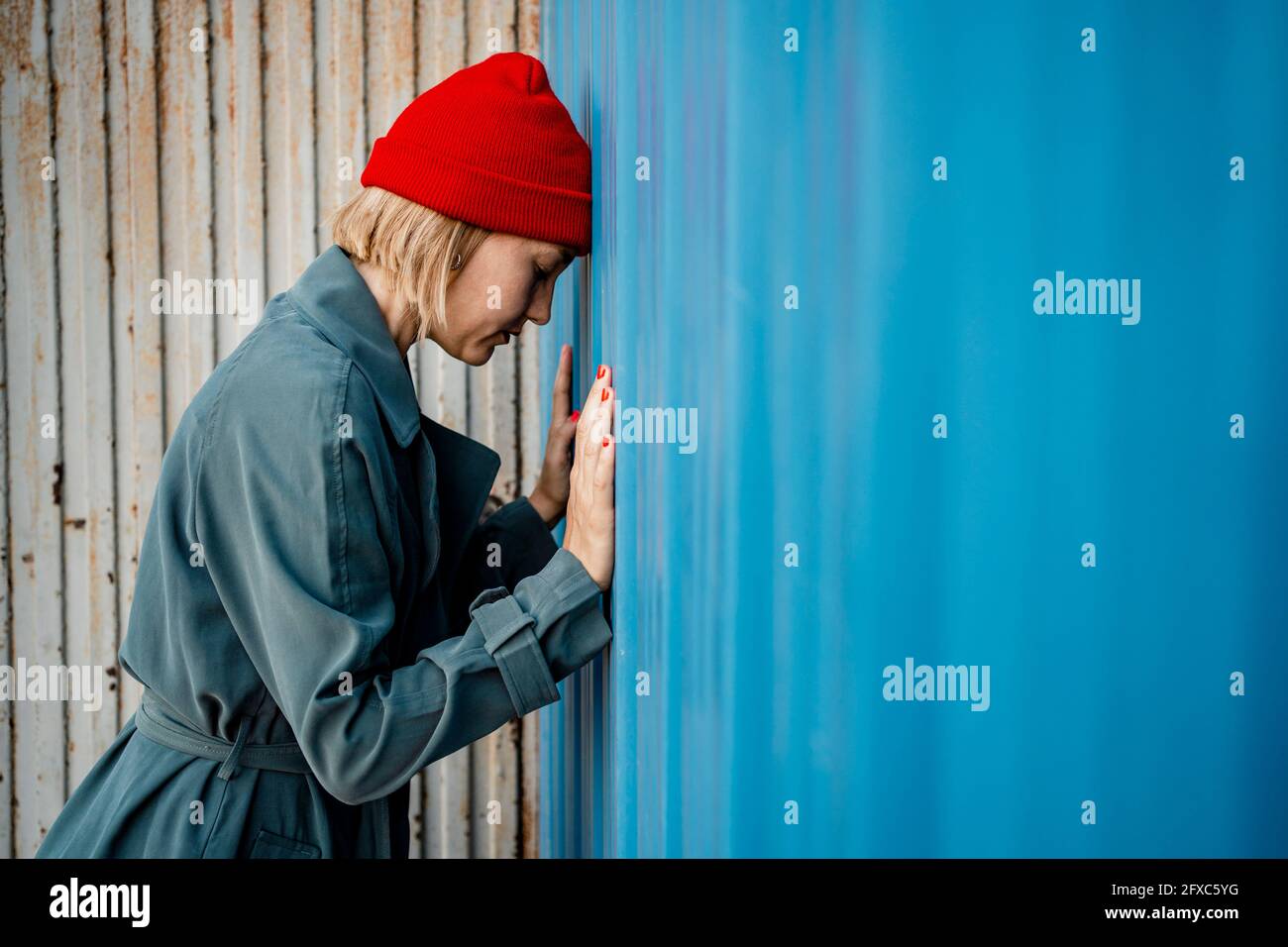Mid adult woman wearing knit hat leaning on blue metal shutter Stock ...