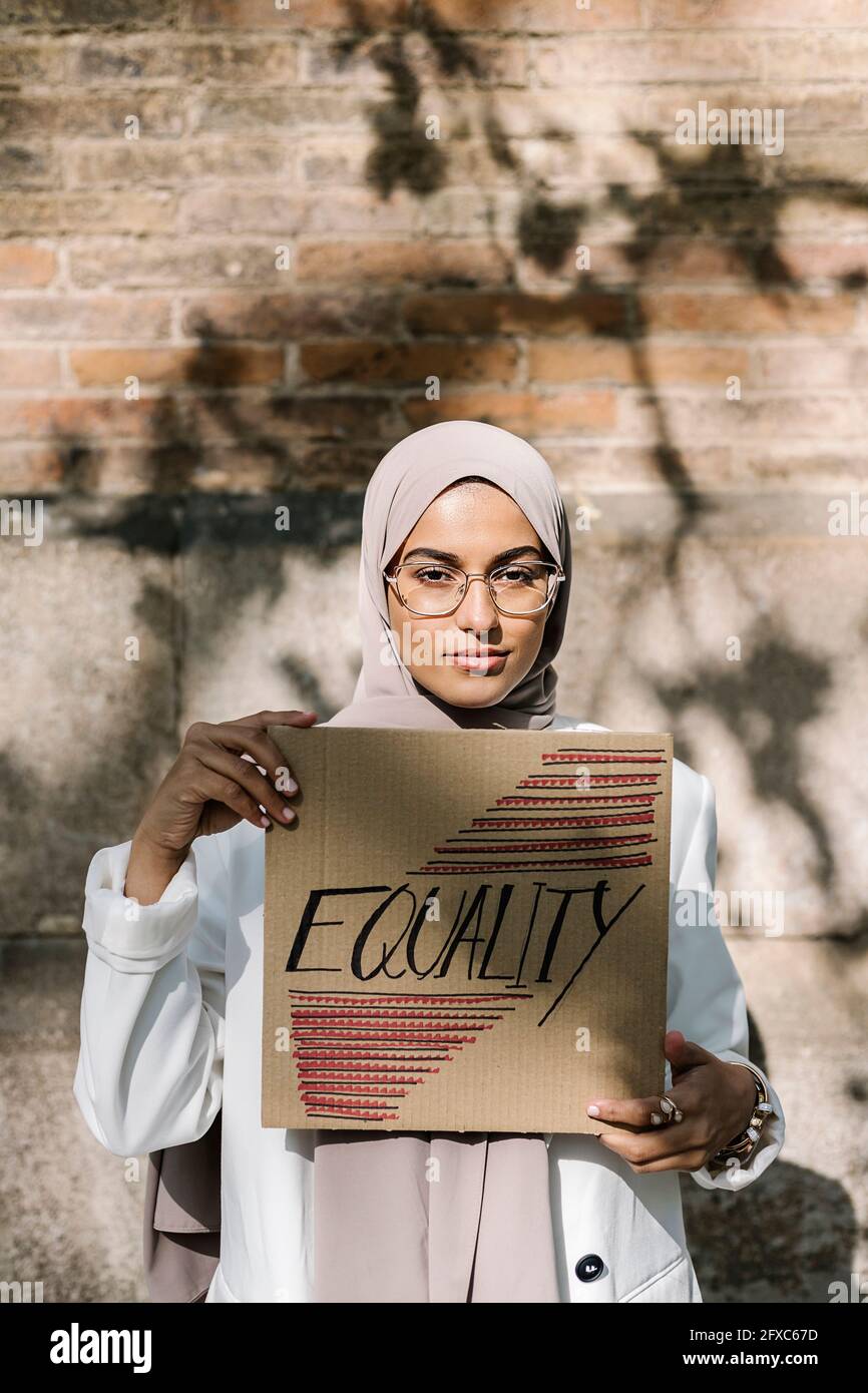 Beautiful woman holding placard with equality text in front of wall ...