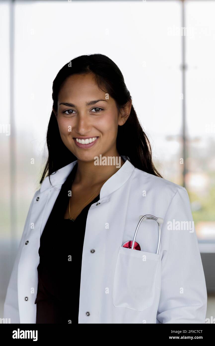 Smiling woman wearing lab coat standing by hospital window Stock Photo ...