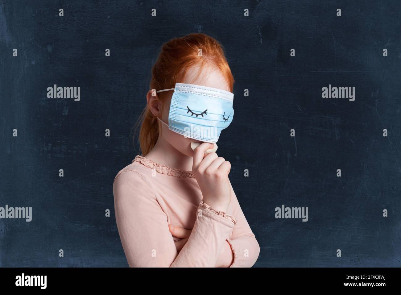Girl eating biscuit while wearing protective face mask against black ...