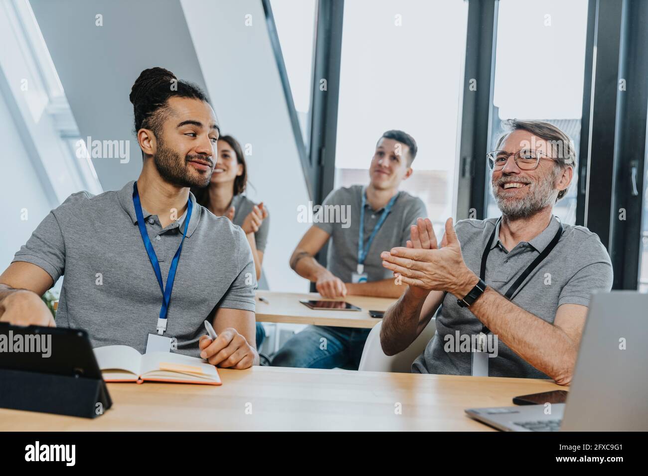 Male trainee looking at smiling colleague clapping while sitting on ...