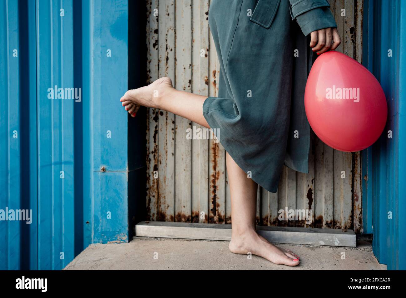 Woman holding red balloon standing on one leg by corrugated shutter ...