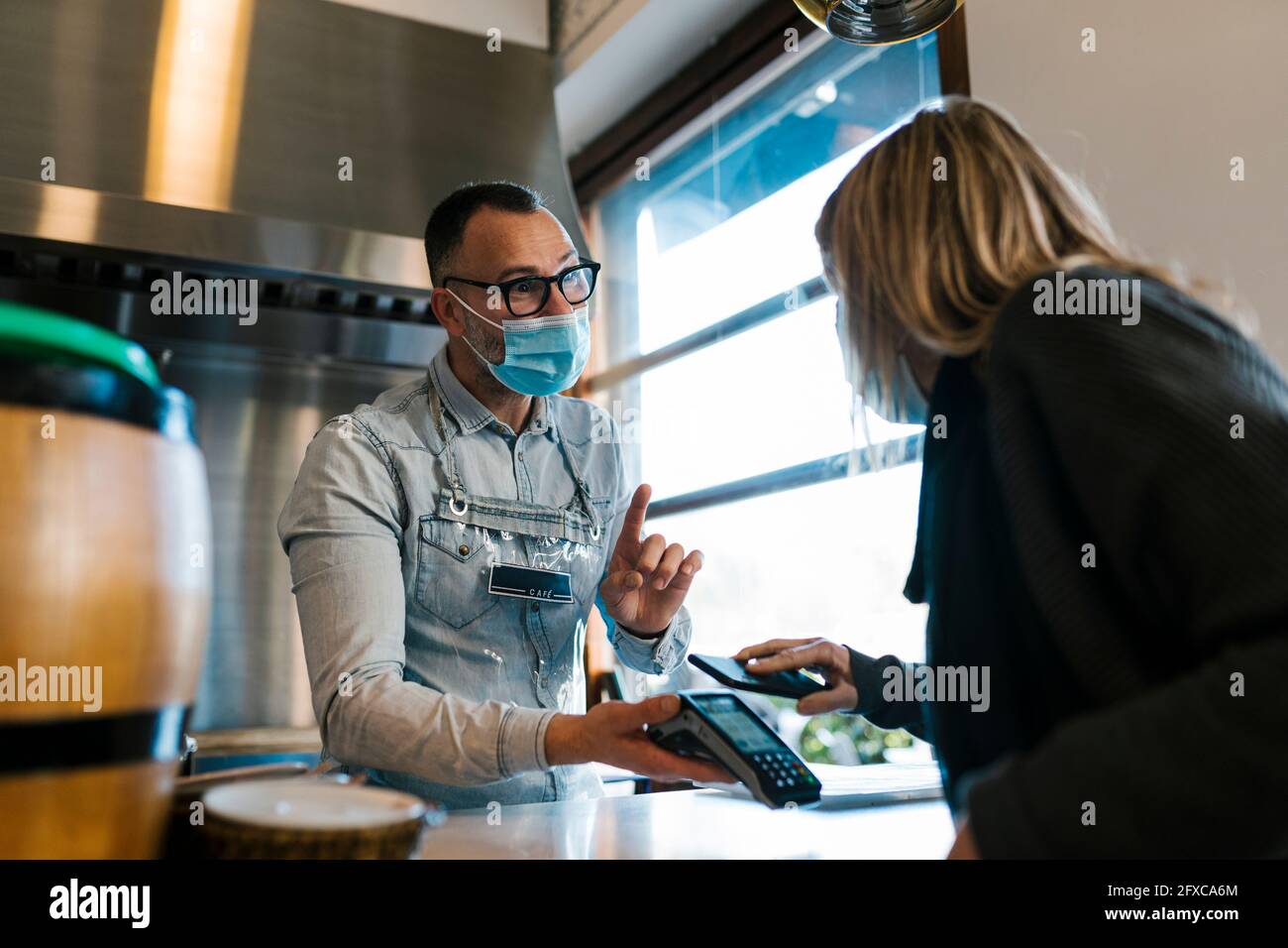 Waiter explaining contactless payment to female customer at a bar ...