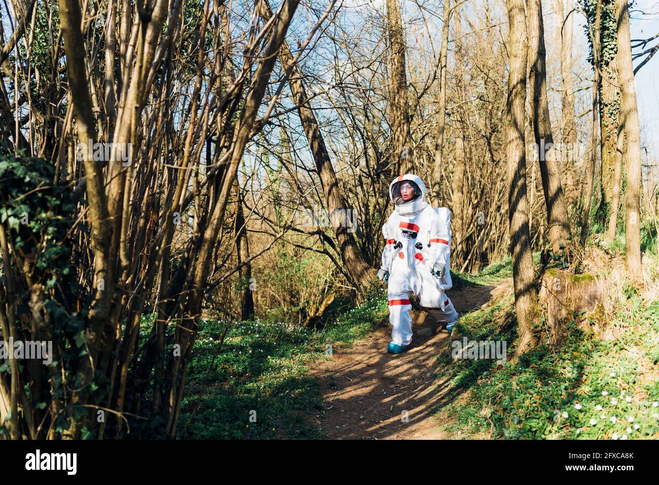 Young female explorer with space suit and helmet walking on forest path ...