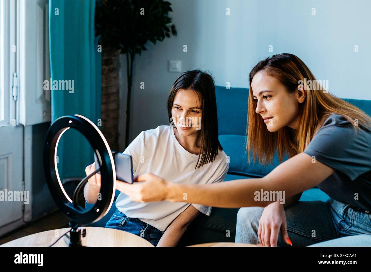 Female roommates adjusting smart phone on ring light while vlogging at ...