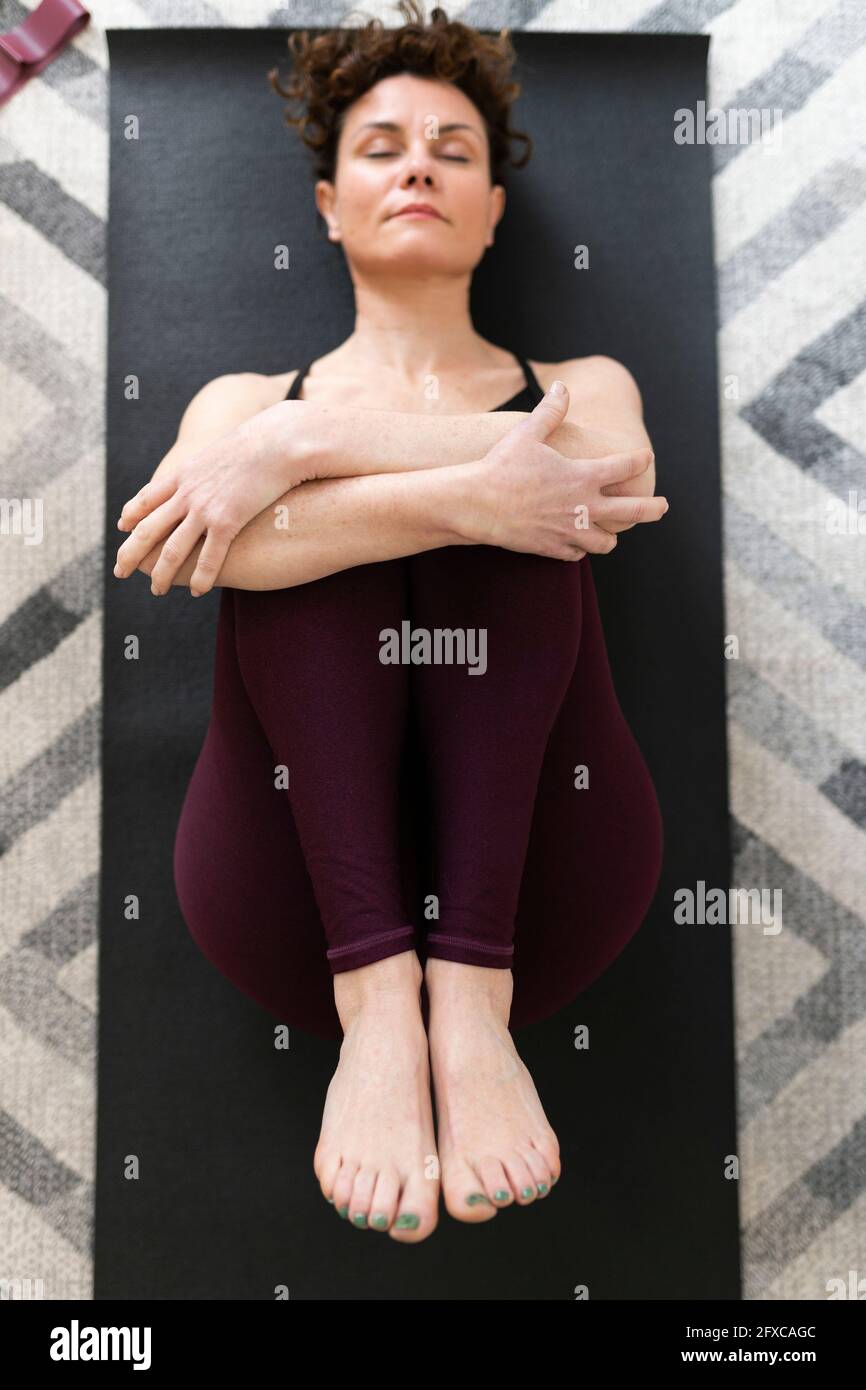 Woman lying on exercise mat in fetal position at home Stock Photo - Alamy