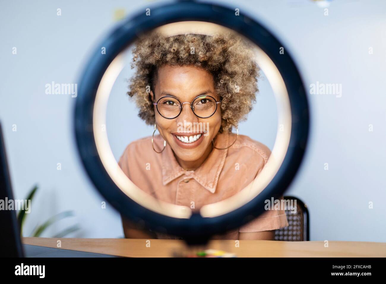 Female influencer with eyeglasses looking through ring light at home ...