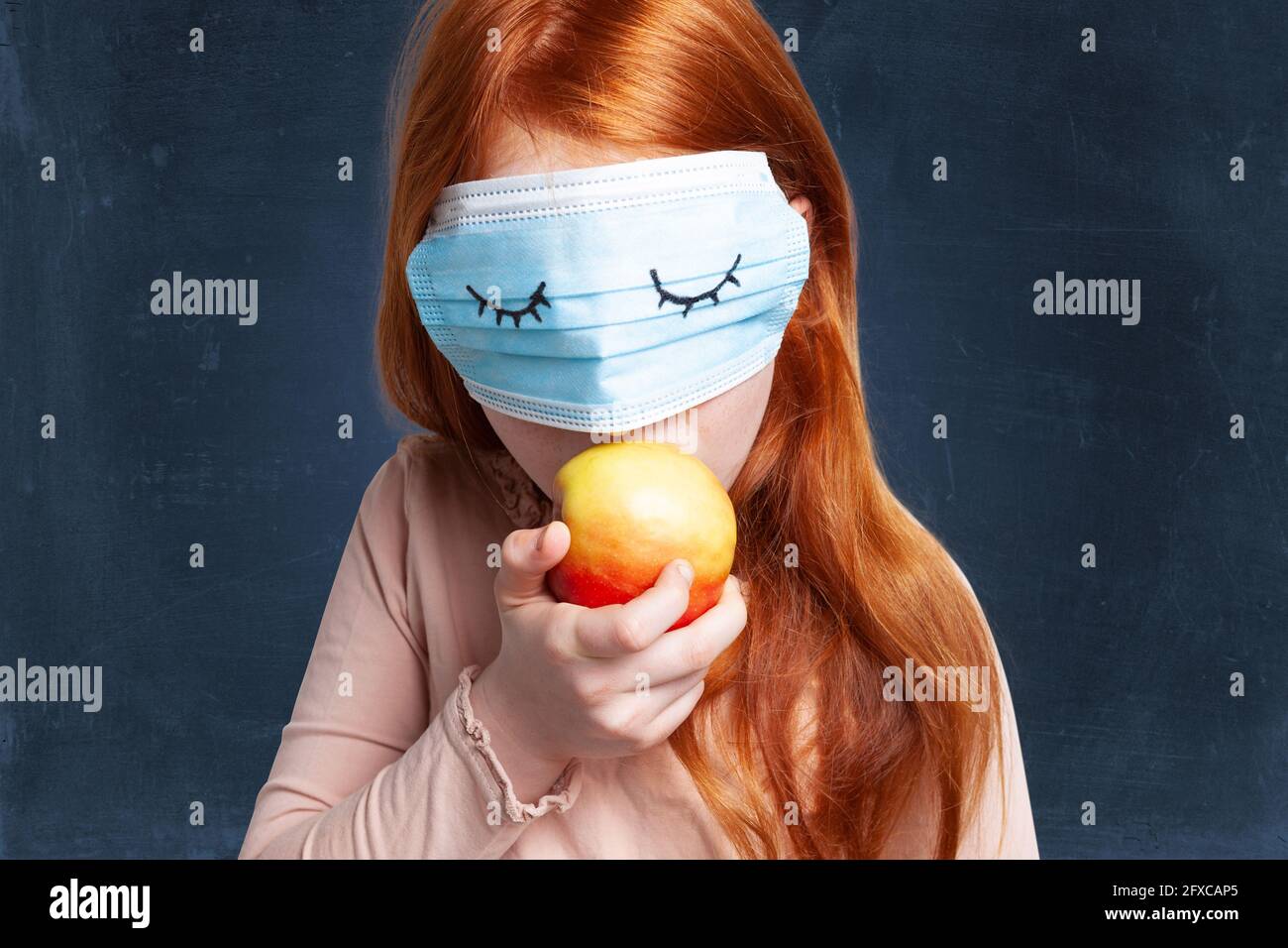 Girl eating apple while covering eyes with protective face mask Stock ...