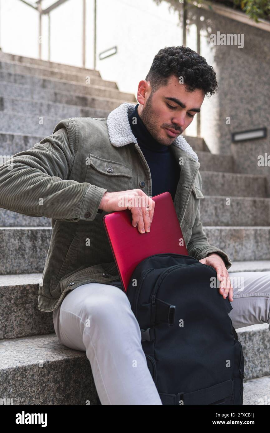 Businessman putting laptop inside backpack while sitting on steps Stock ...