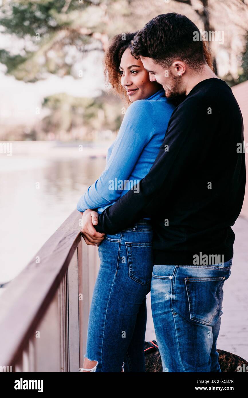 Smiling man embracing girlfriend in front of railing Stock Photo - Alamy