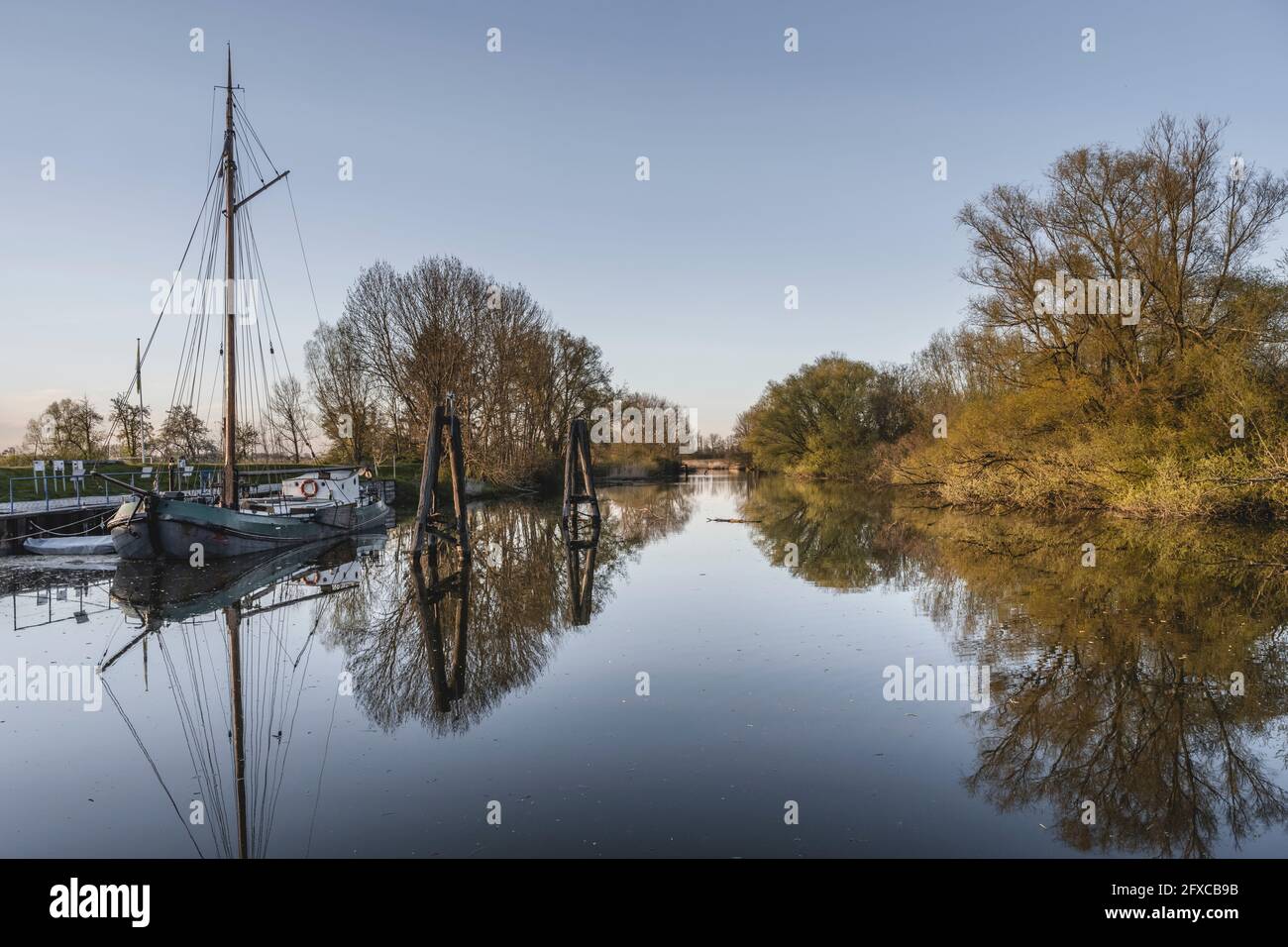 Germany, Altes Land, Jork, Trees and sailboat reflecting in waters of ...