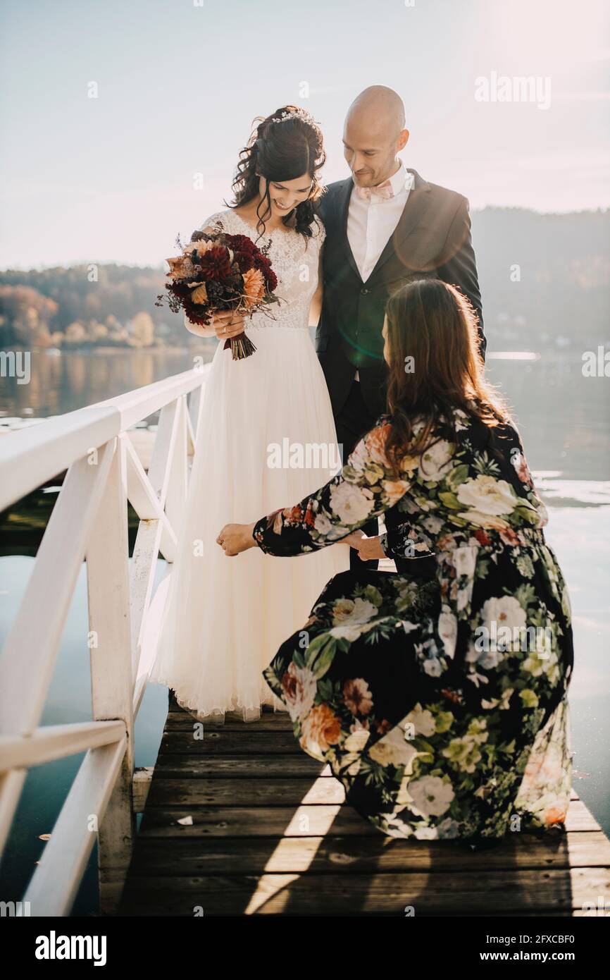 Bridesmaid helping wedding couple on jetty over lake Stock Photo - Alamy