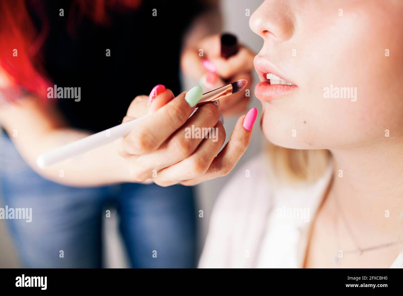 Female make-up artist applying lipstick to model in studio Stock Photo ...