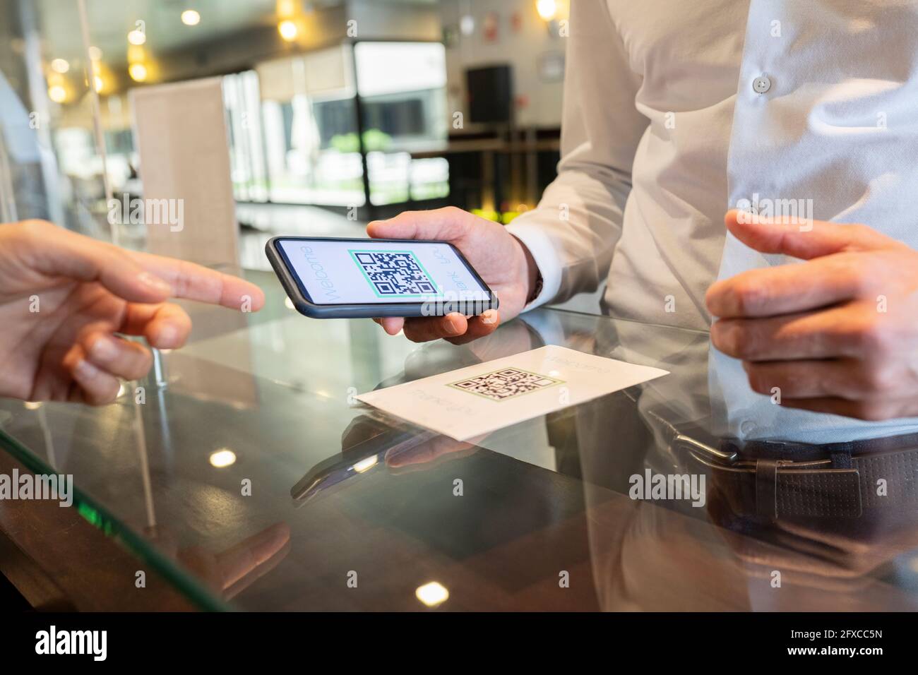 Mature man showing QR code on mobile phone at receptionist hotel desk ...