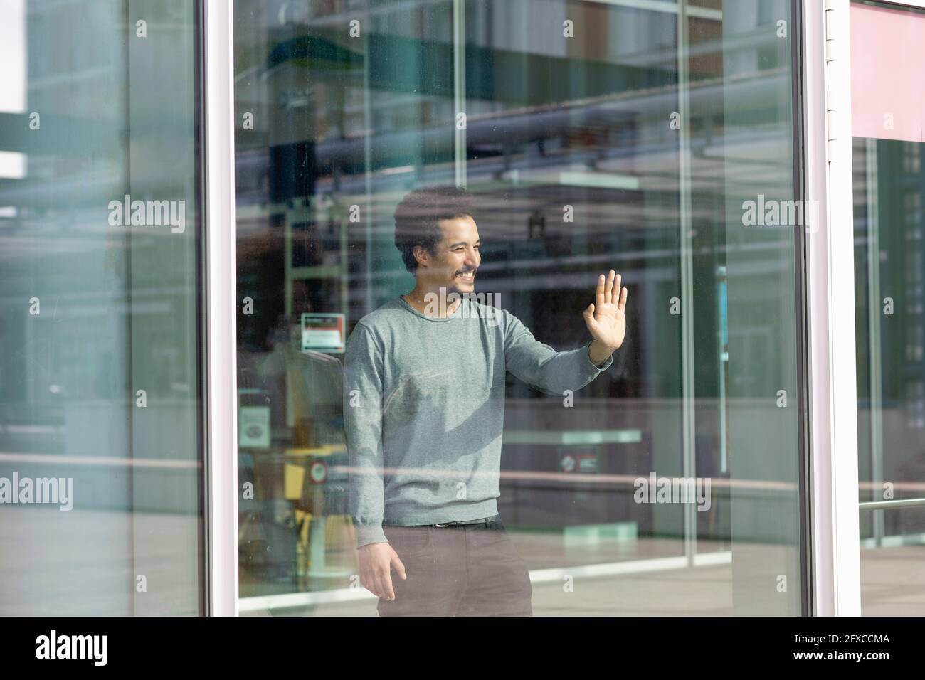 Smiling man looking away while touching glass wall Stock Photo - Alamy