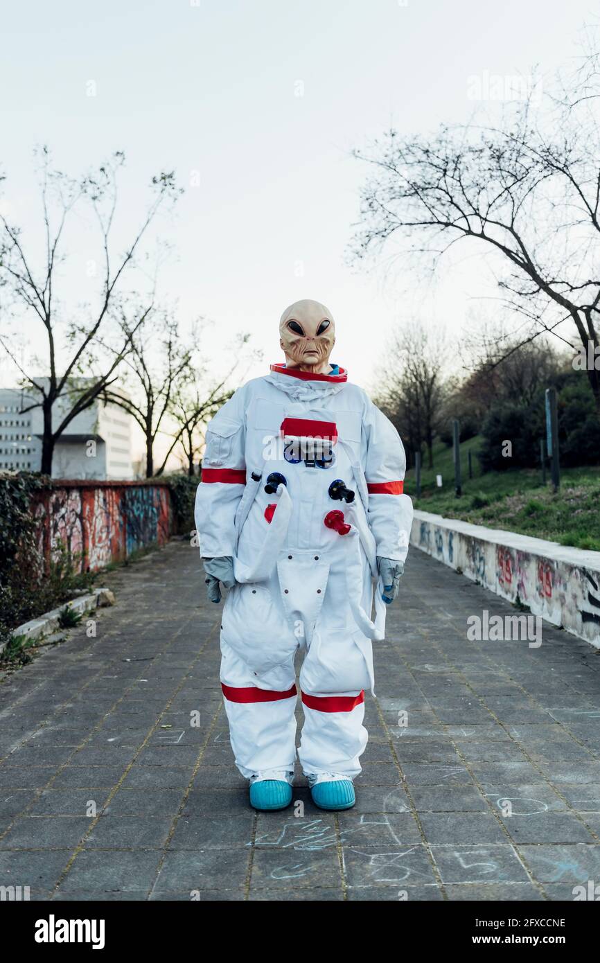 Young female astronaut wearing alien mask while standing on footpath ...